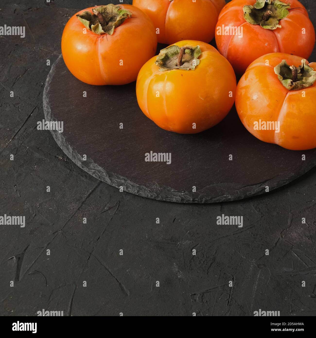 Group of fresh orange ripe persimmon fruits laying on round black slate ...