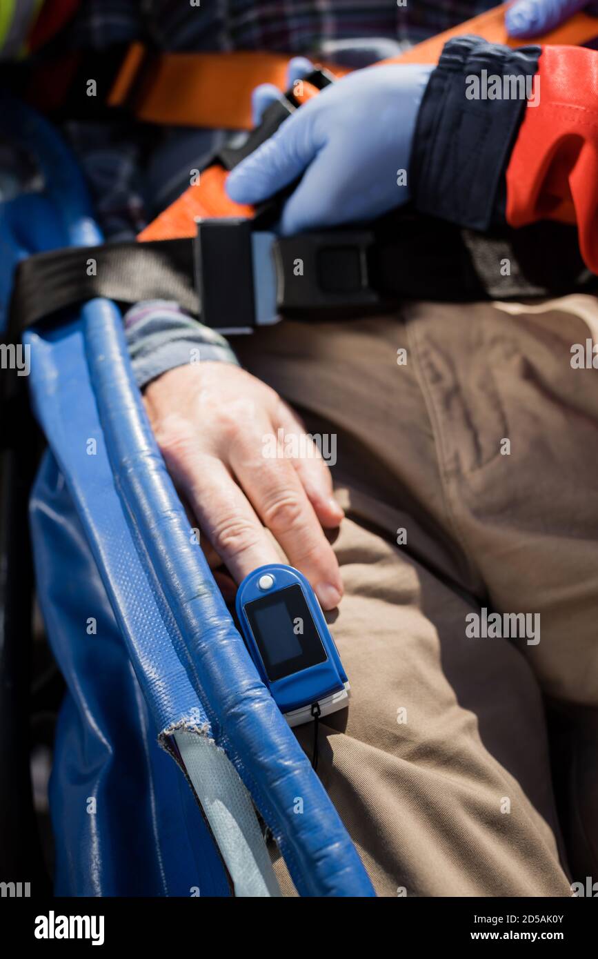 Cropped view of paramedic in latex gloves locking belt of stretcher ...