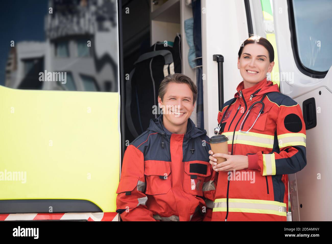 Paramedics with coffee to go looking at camera near ambulance car ...