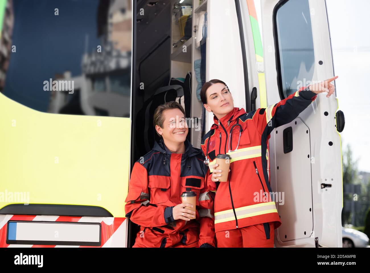 Paramedic pointing with finger near colleague with coffee to go and ...