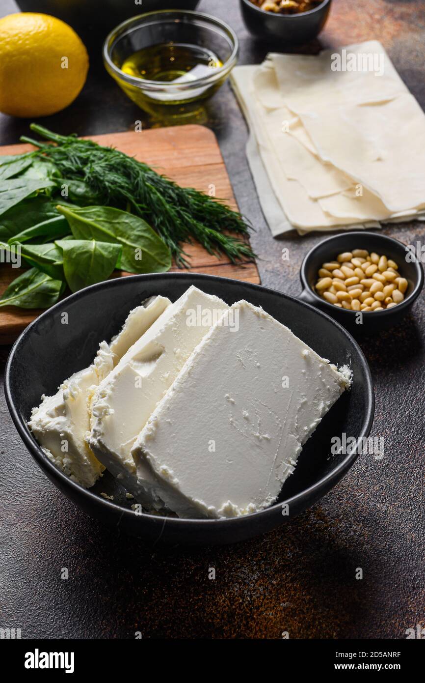 Traditional feta cheese in black bowl side view in front of ingredients ...
