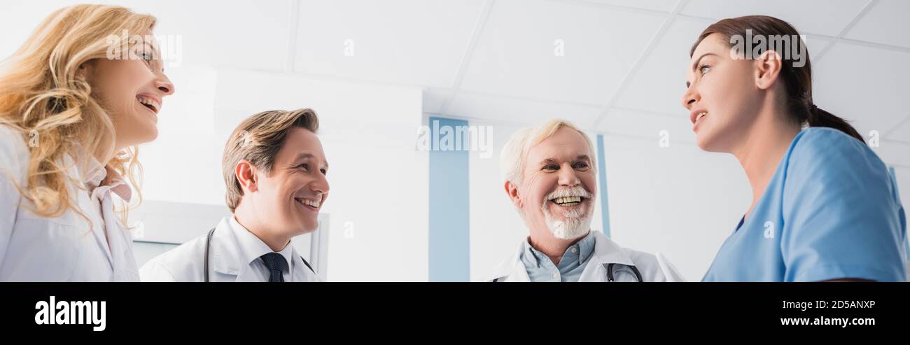 Panoramic shot of doctors looking at nurse while talking in clinic ...