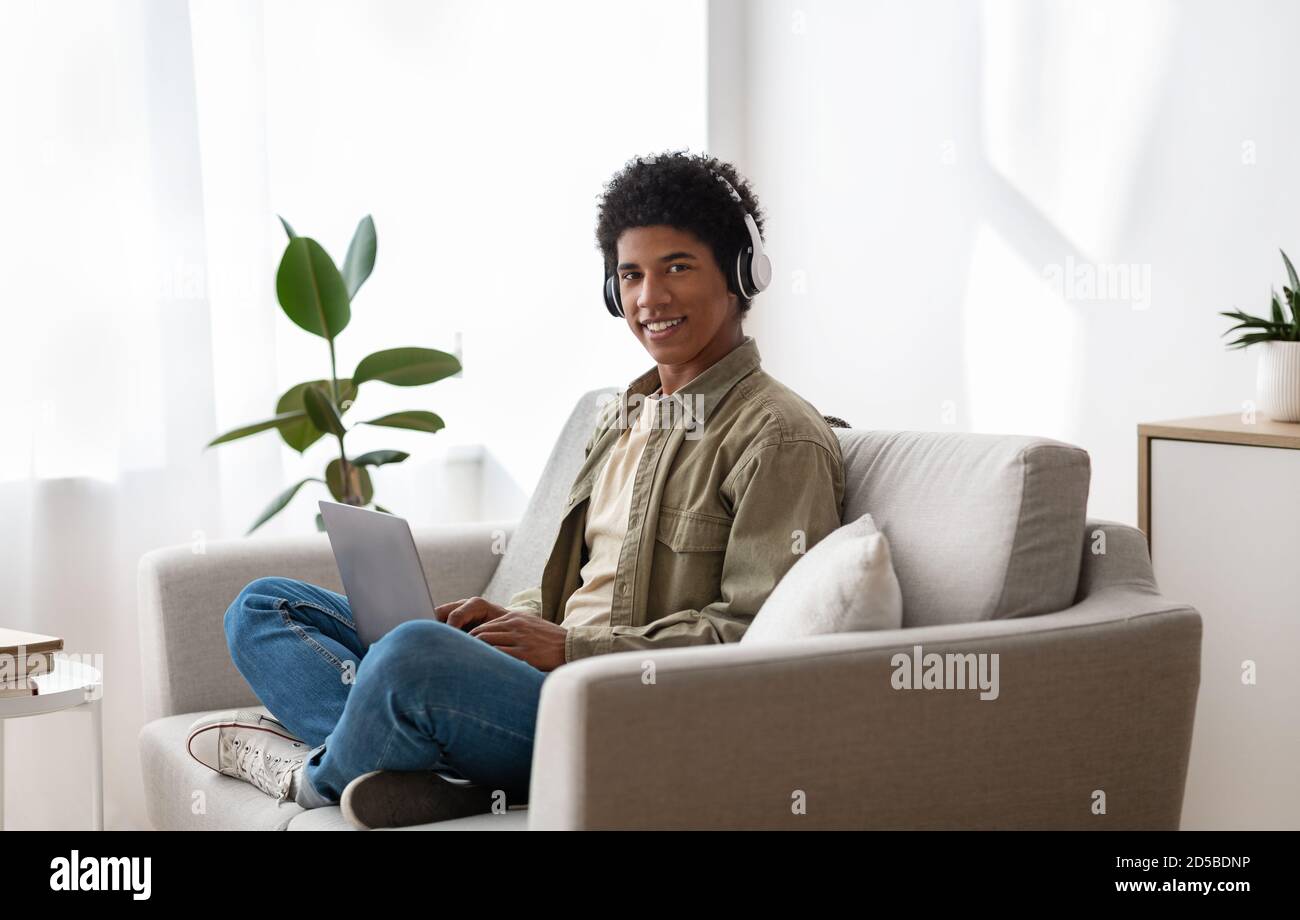 Portrait of black teen guy with laptop and headphones participating in ...