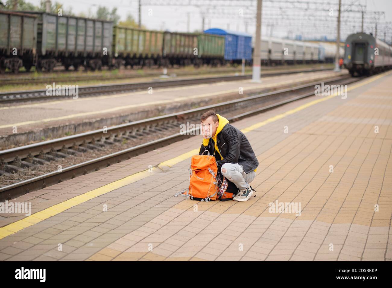Young man squats on platform, waiting for train. Male passenger with ...