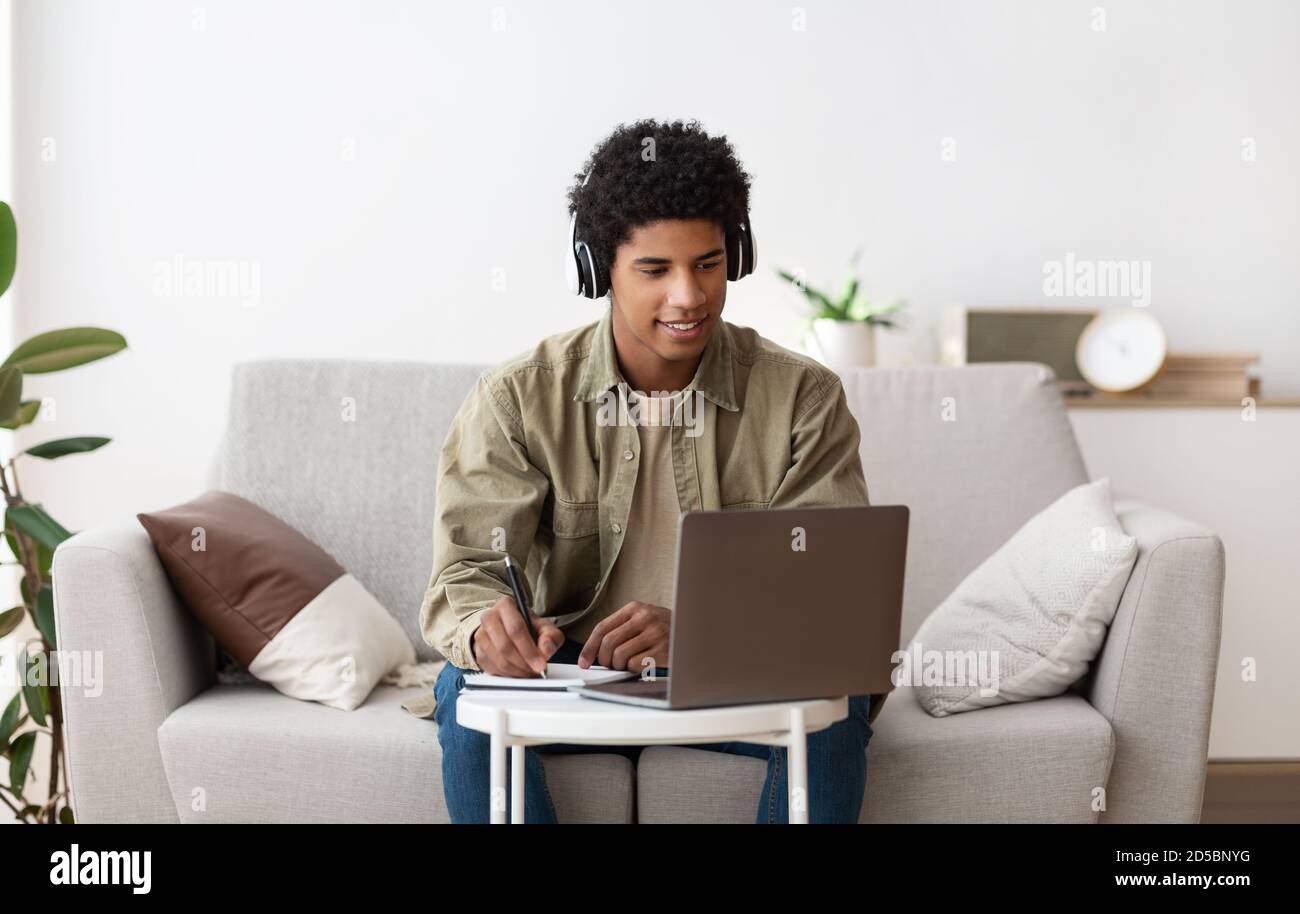 Web-based education concept. Happy teen guy in headset taking notes ...