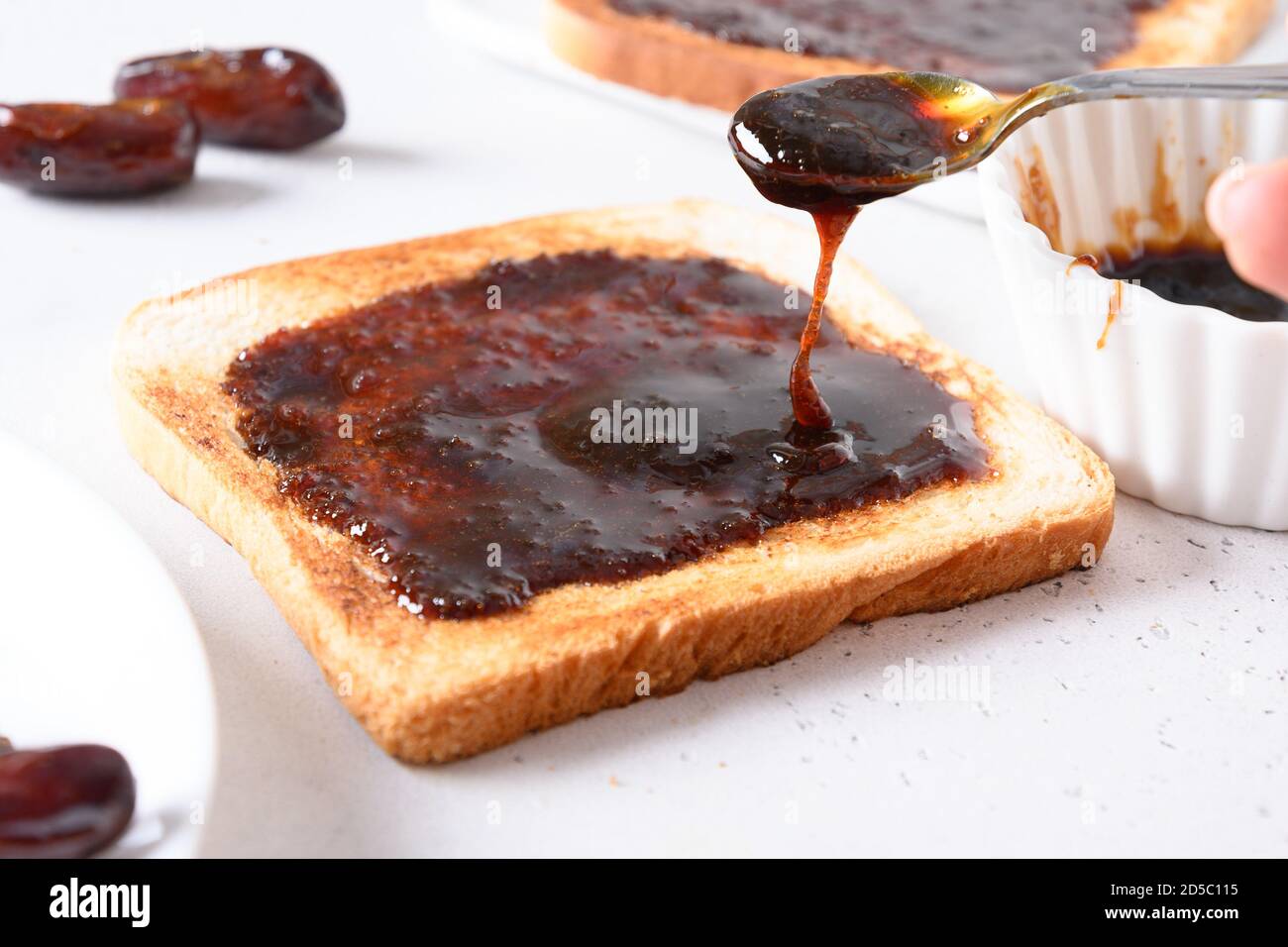 Woman pouring dates jam on fresh crispy toast on white. Close up Stock ...