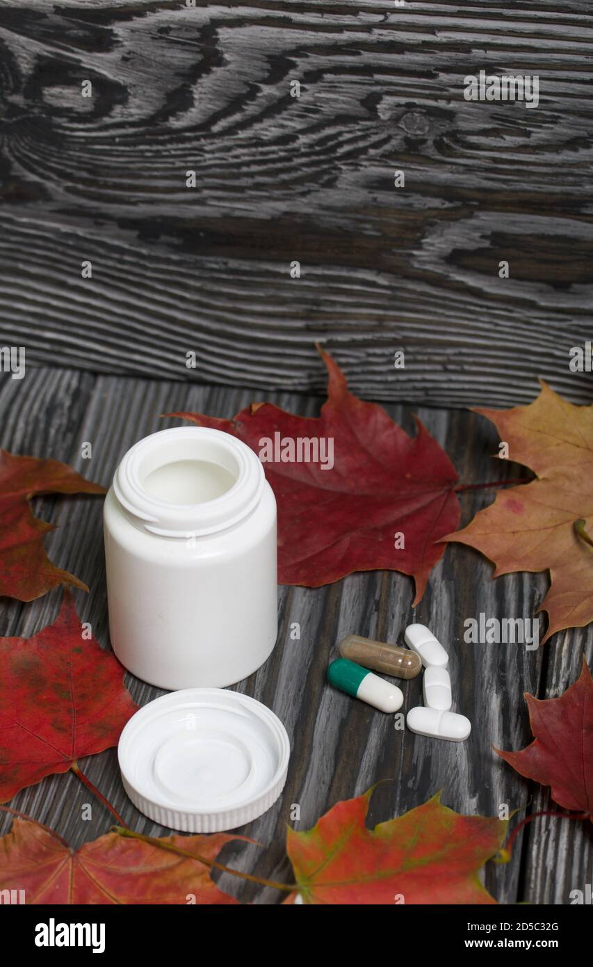 Container with pills and autumn maple leaves. The lid of the container ...