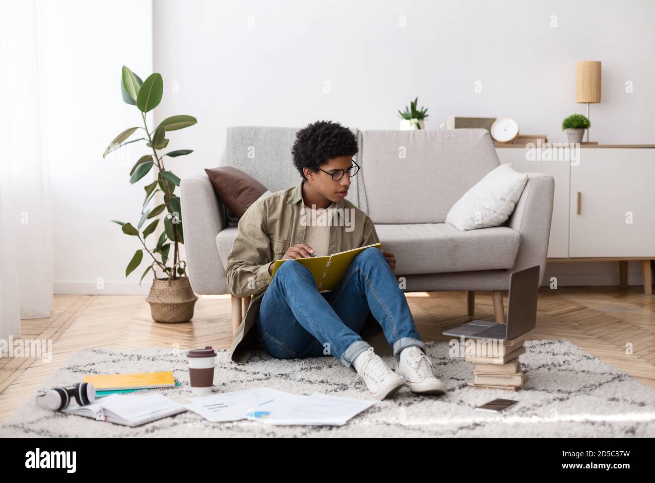 Focused black teen student taking notes during his online lesson on ...
