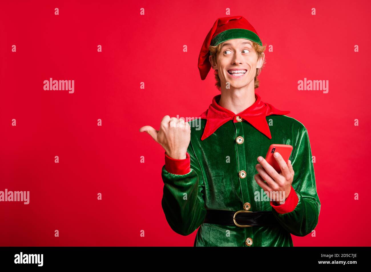 Funky elf guy in green cap hold smartphone point thumb finger empty ...