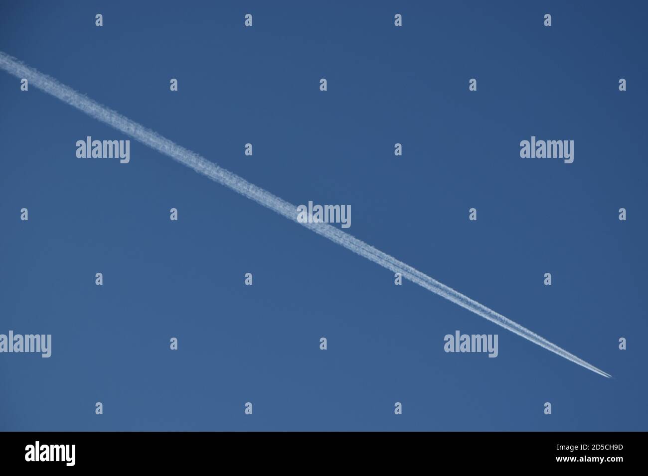 A single plane flies across the blue sky. Jet traili on blue sky ...