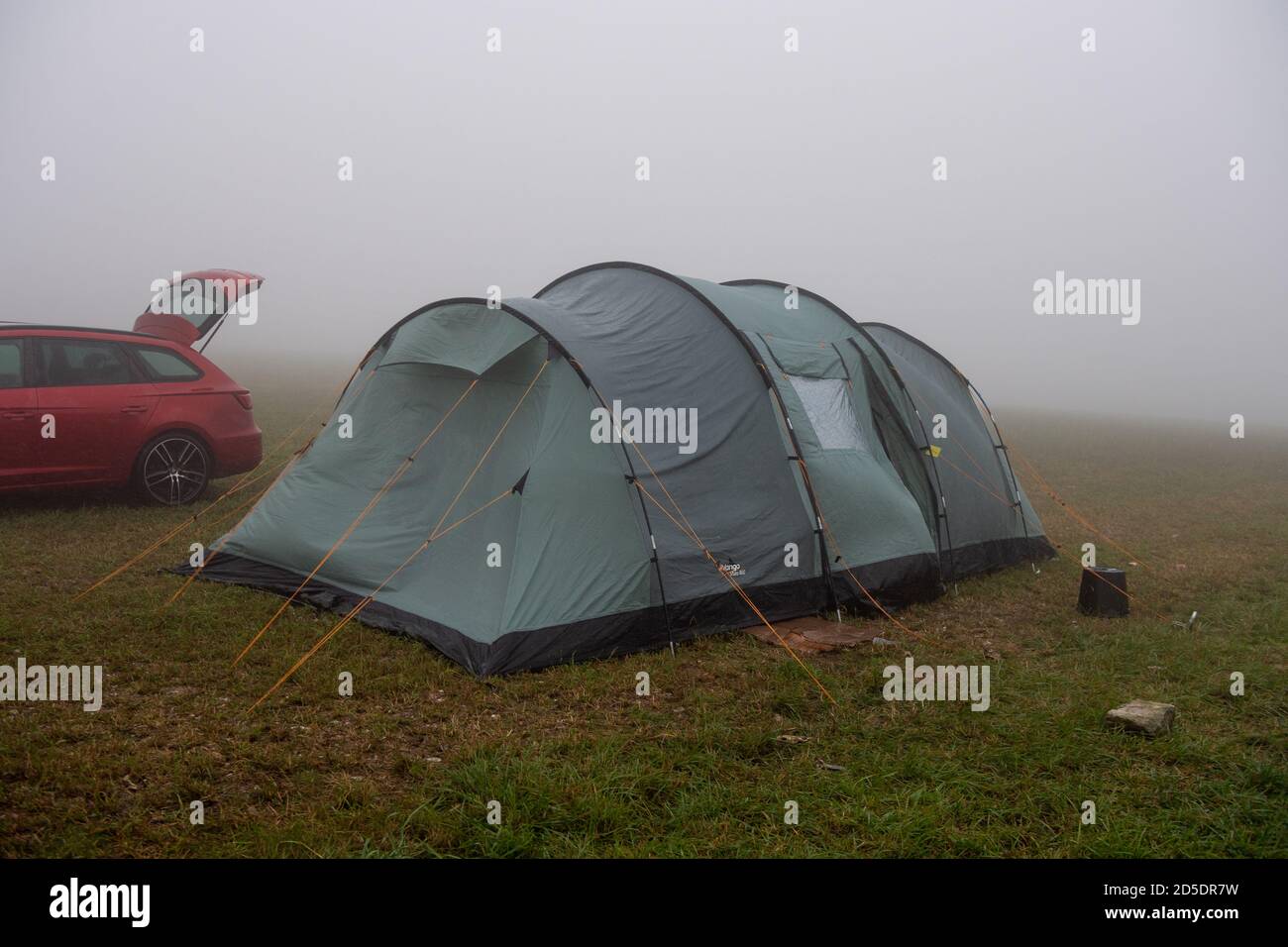 A single tent next to a car in a field in bad UK weather of fog and ...