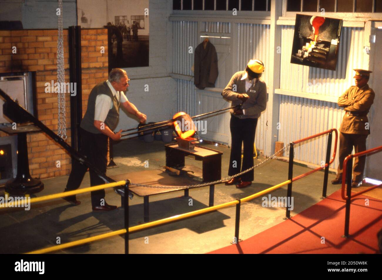 Two men pouring molten gold into a mould to make a bullion bar block ...