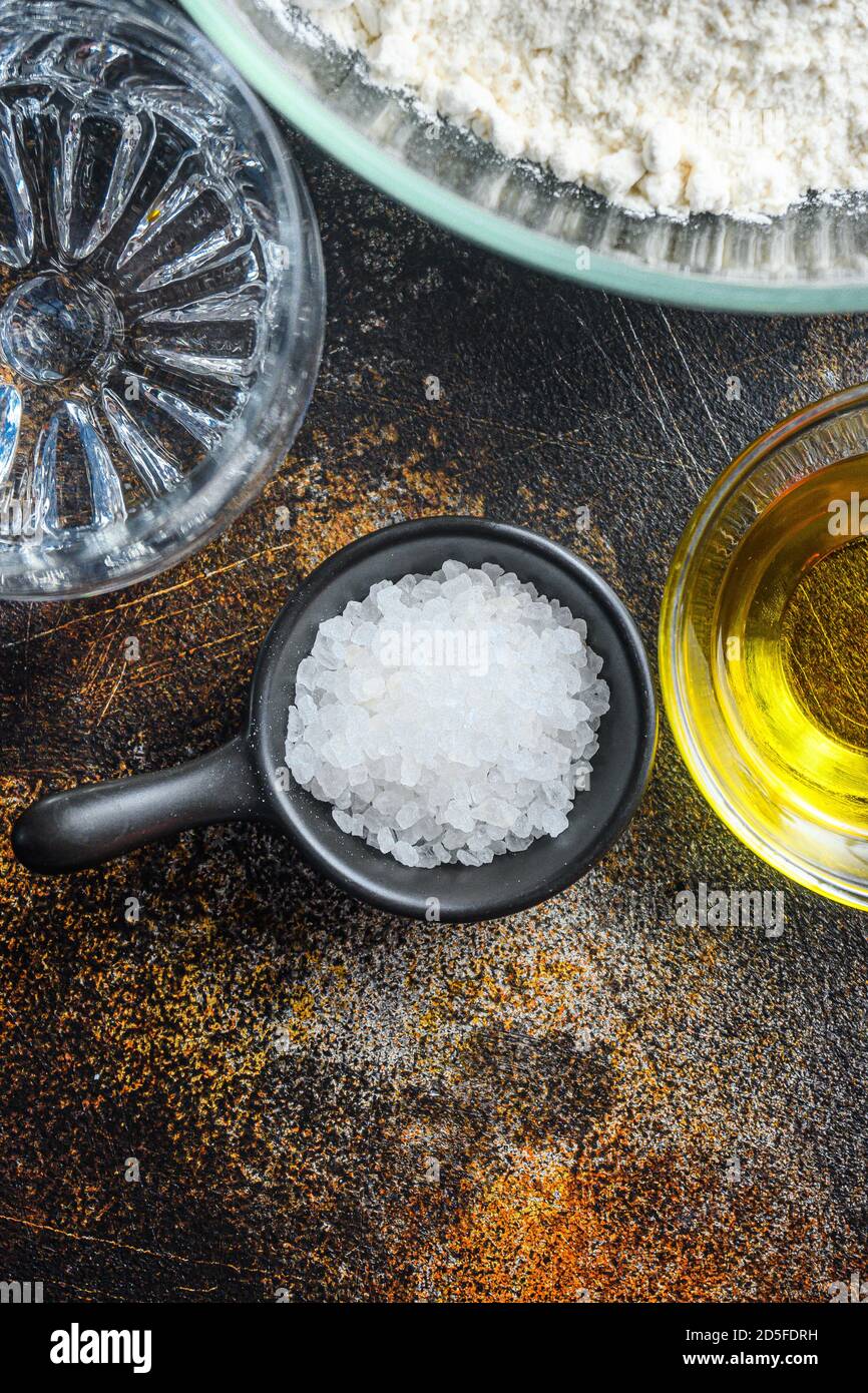 Ingredients for the dough, flour oil water and salt on darkbackground ...