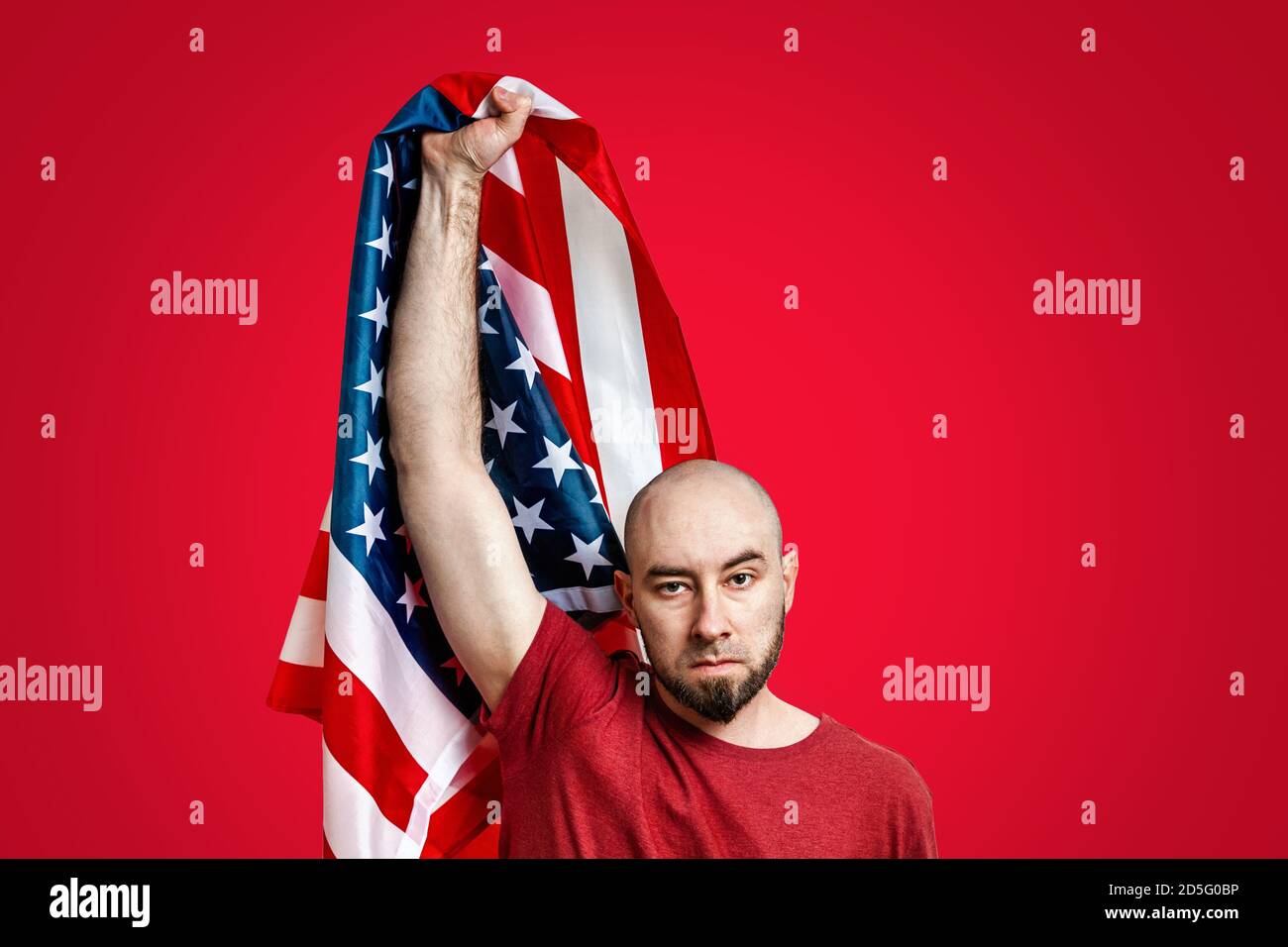 A Caucasian man with a serious face holds up an American flag with one ...
