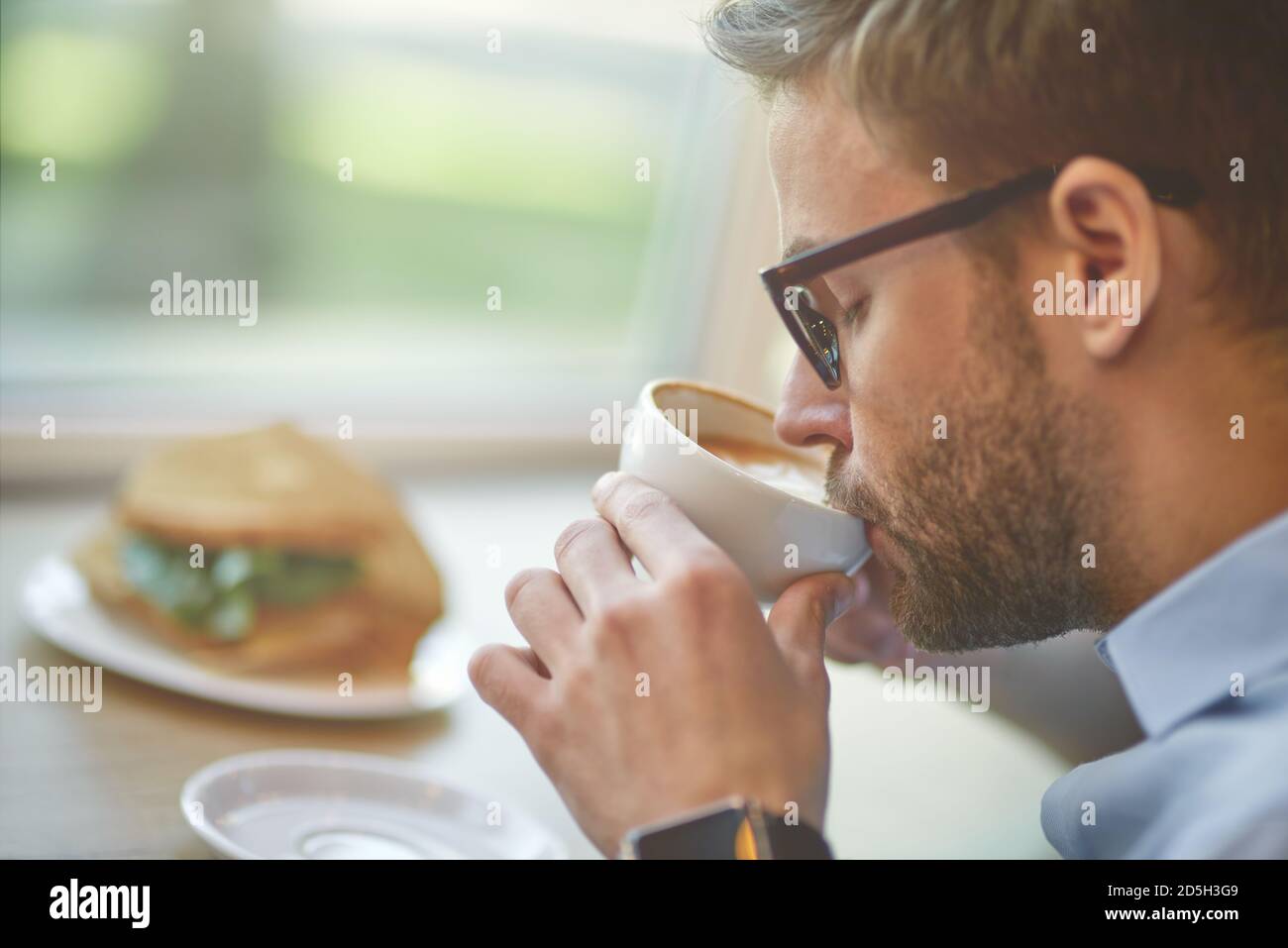 Side view of a young man drinking coffee cappuccino while sitting in ...