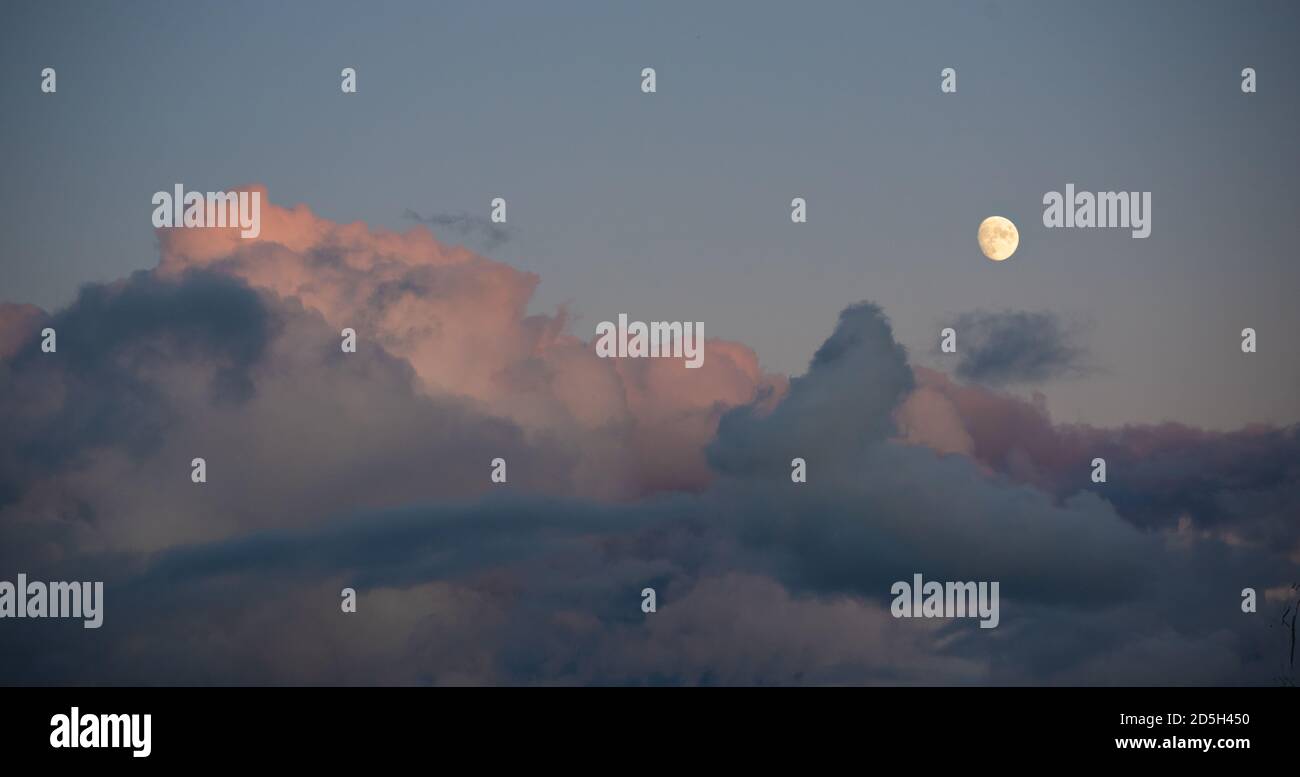 Bright moon rising in the clouds illuminated by sunset Stock Photo - Alamy