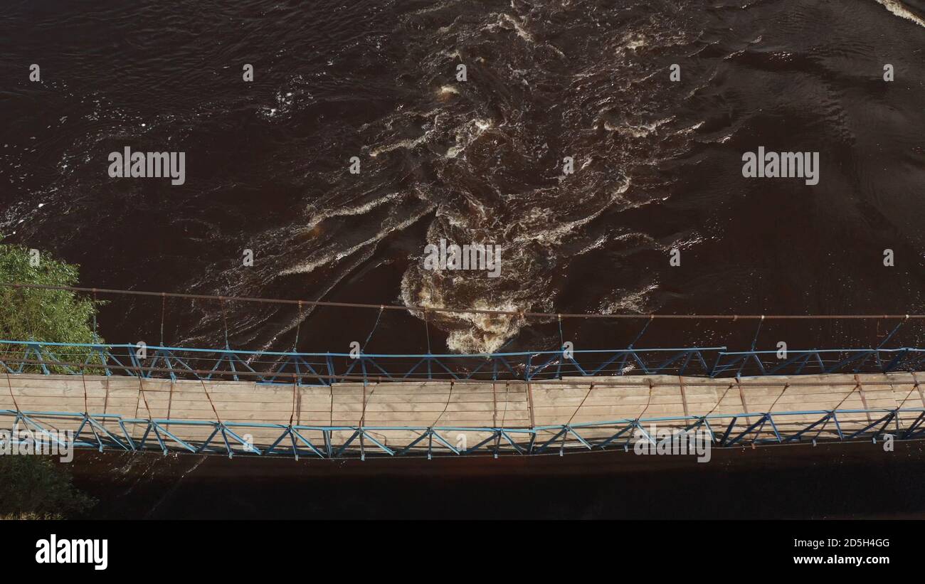 Suspended footbridge across the river. Suspended wooden pedestrian ...