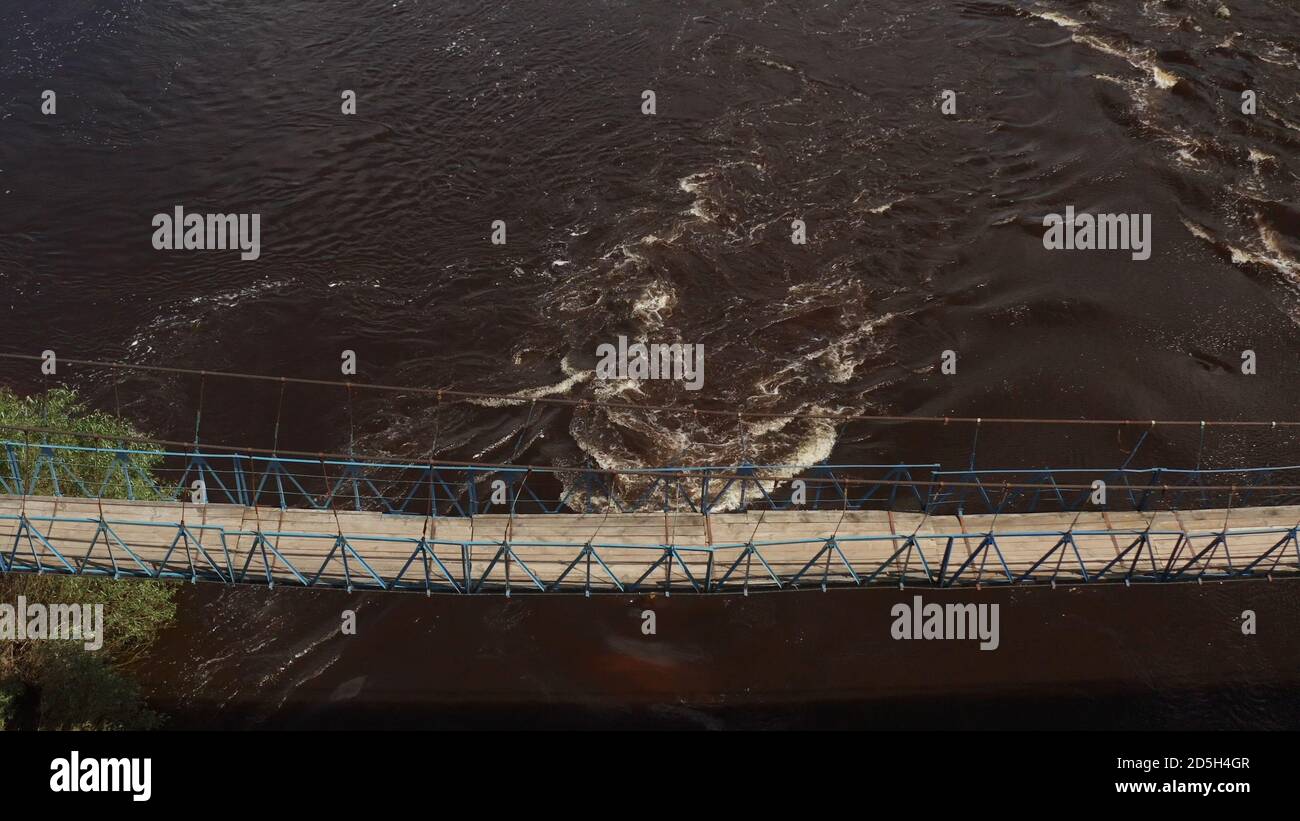 Suspended footbridge across the river. Suspended wooden pedestrian ...