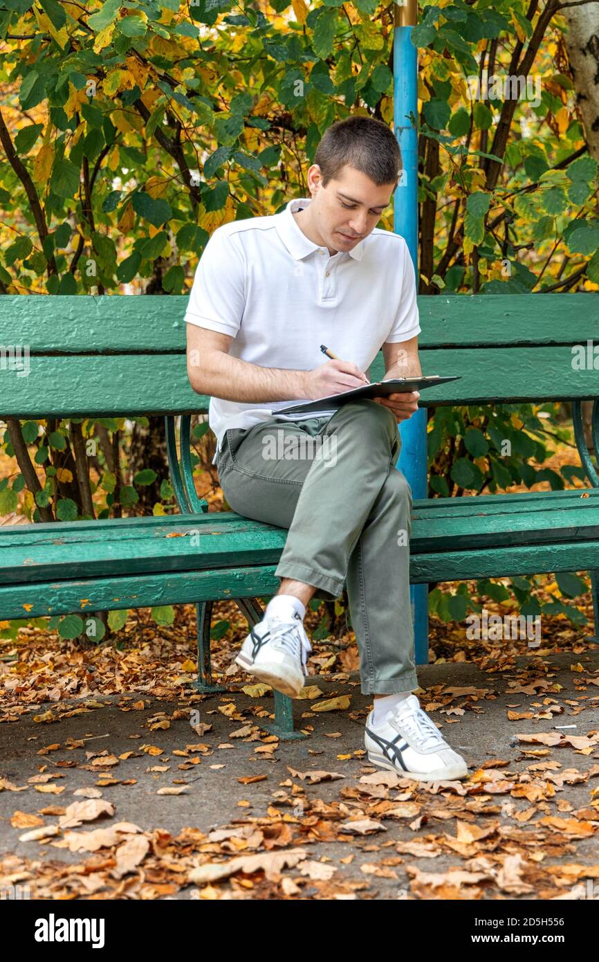 man writes in a notebook on his knee while sitting on the bench Stock ...