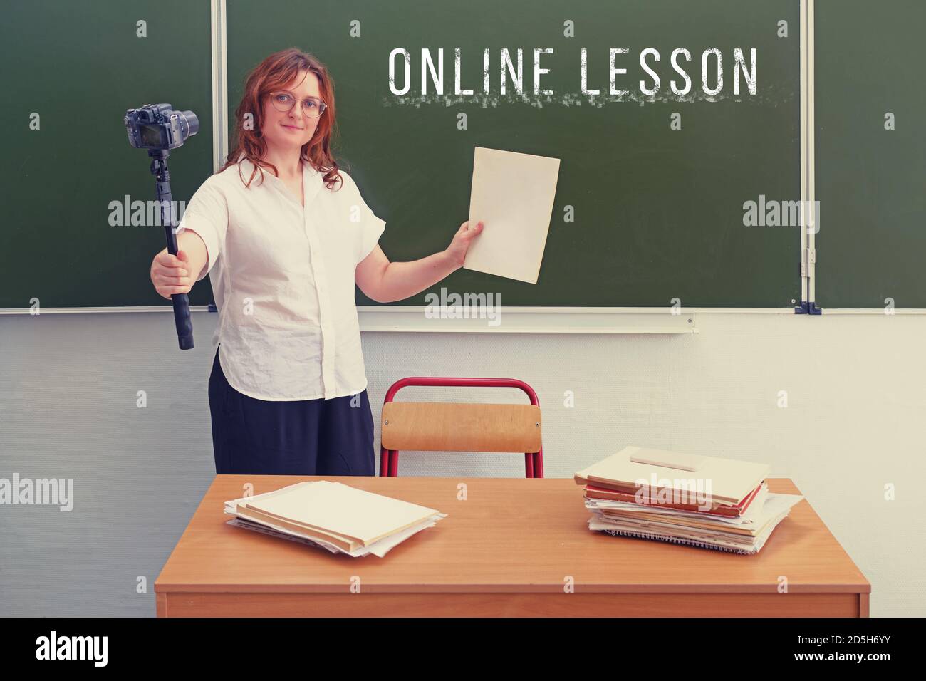 A school teacher holds a camera on a tripod standing at the blackboard ...