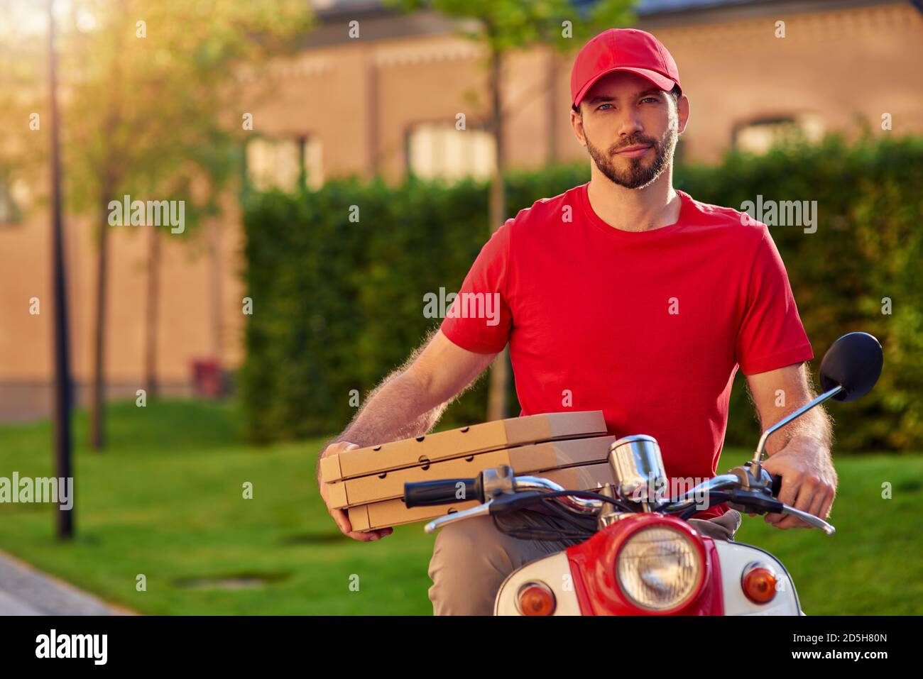 Young handsome caucasian delivery man in uniform on scooter holding ...