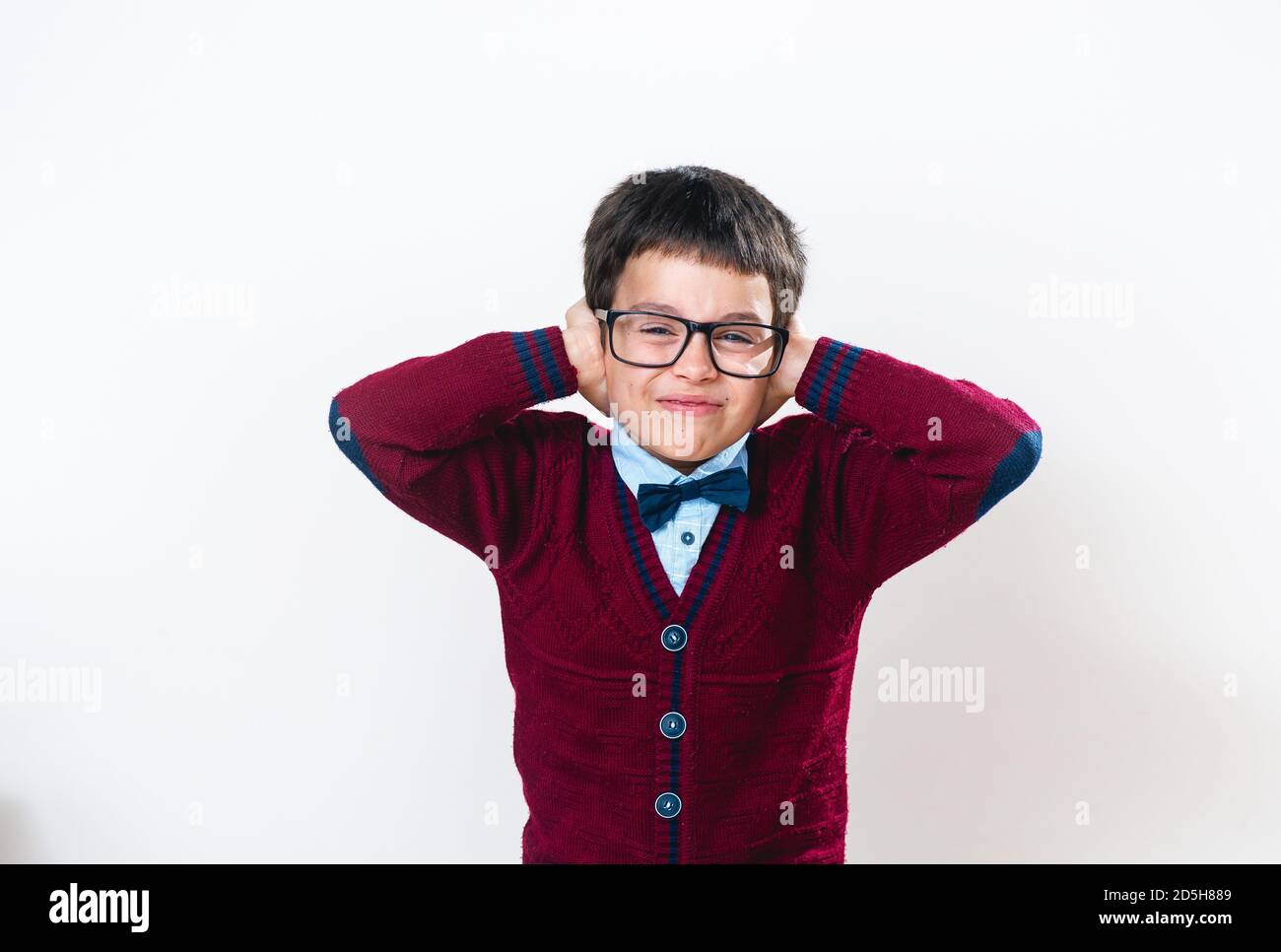 The schoolboy in glasses and a red sweater is covering his ears with ...