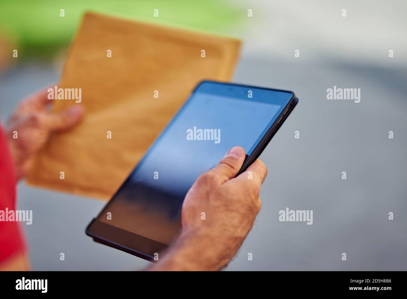 Digital tablet and paper packet in hands of delivery man outdoors ...