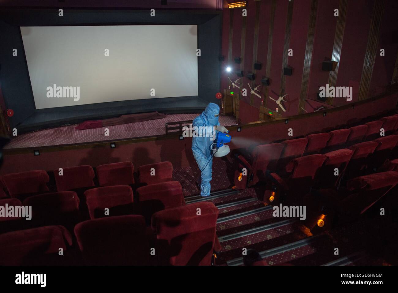 A worker wearing a personal protective suit PPE disinfecting the seats ...