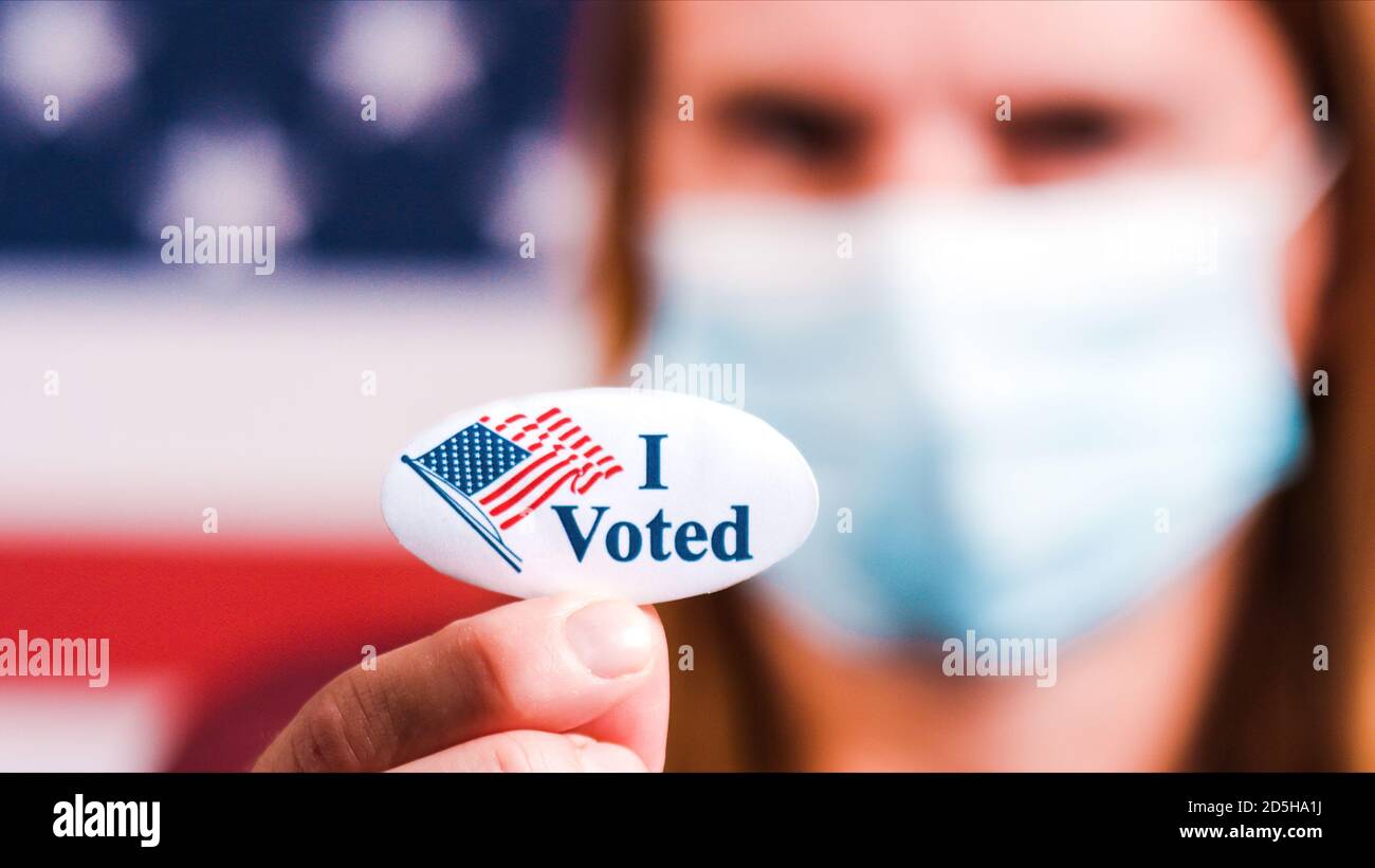 Woman with face mask showing I voted sticker with american flag ...