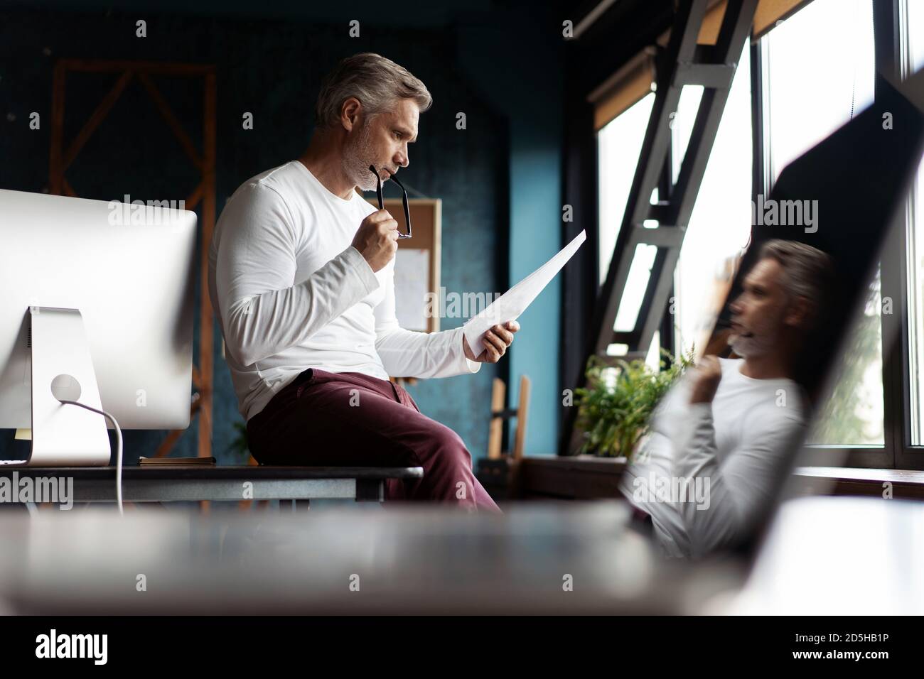 Casual Grey-haired Mature man reading paper in his office Stock Photo ...