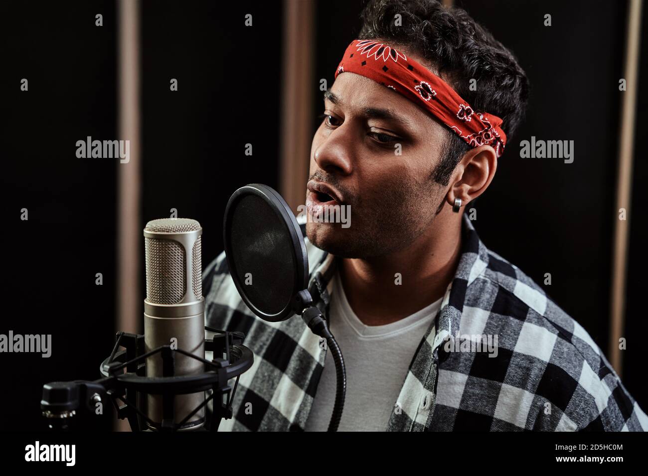 Portrait of young man, hip hop artist singing into a condenser ...