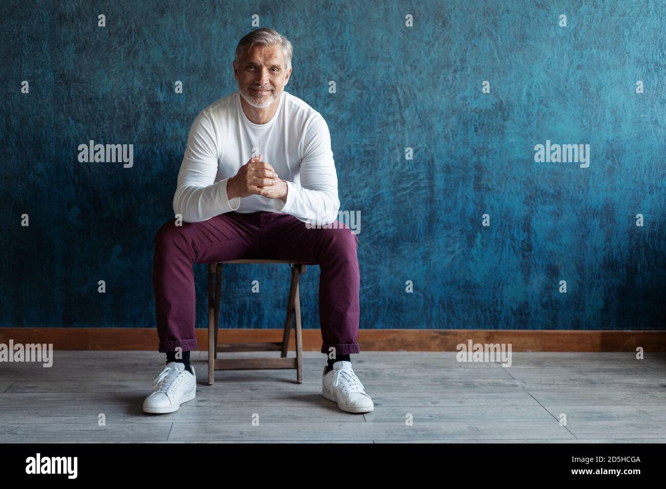 Portrait of a casual Grey-haired Mature handsome man sitting on a chair ...