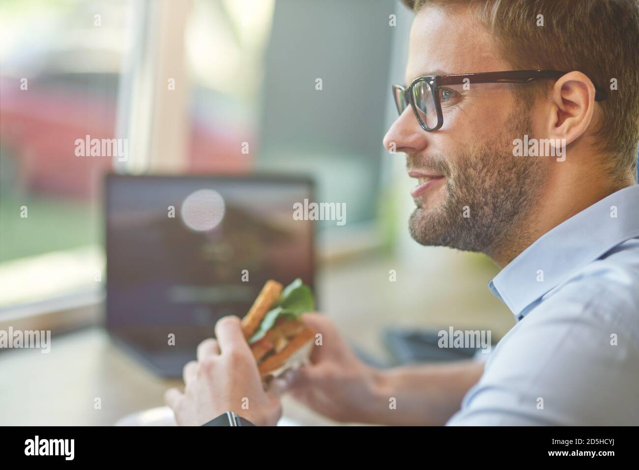 Side view of a young happy businessman sitting at wooden table in cafe ...