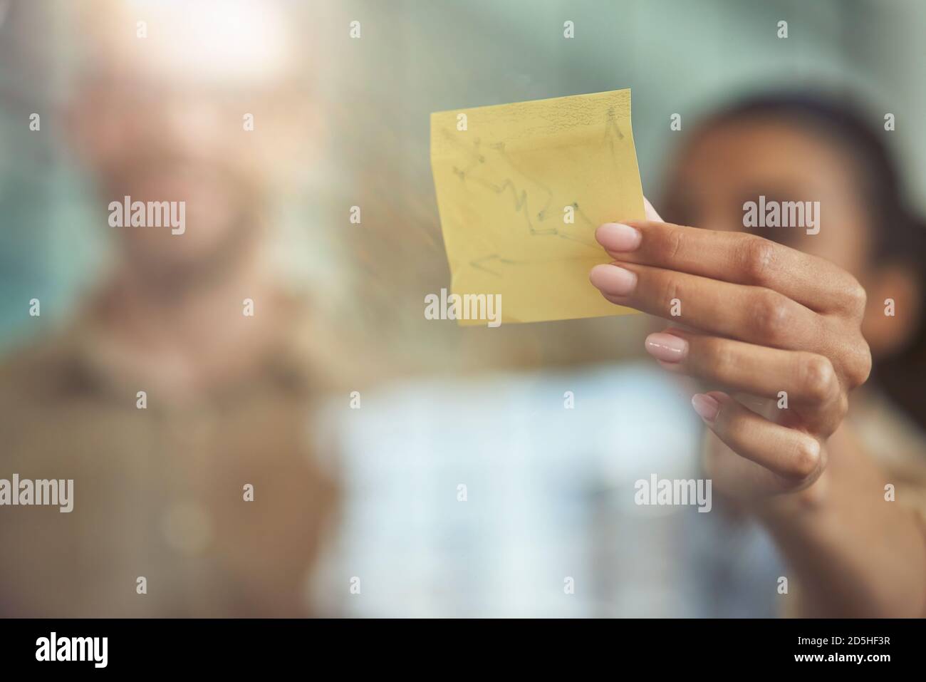 Young mixed race woman putting colorful sticky note on a glass wall ...