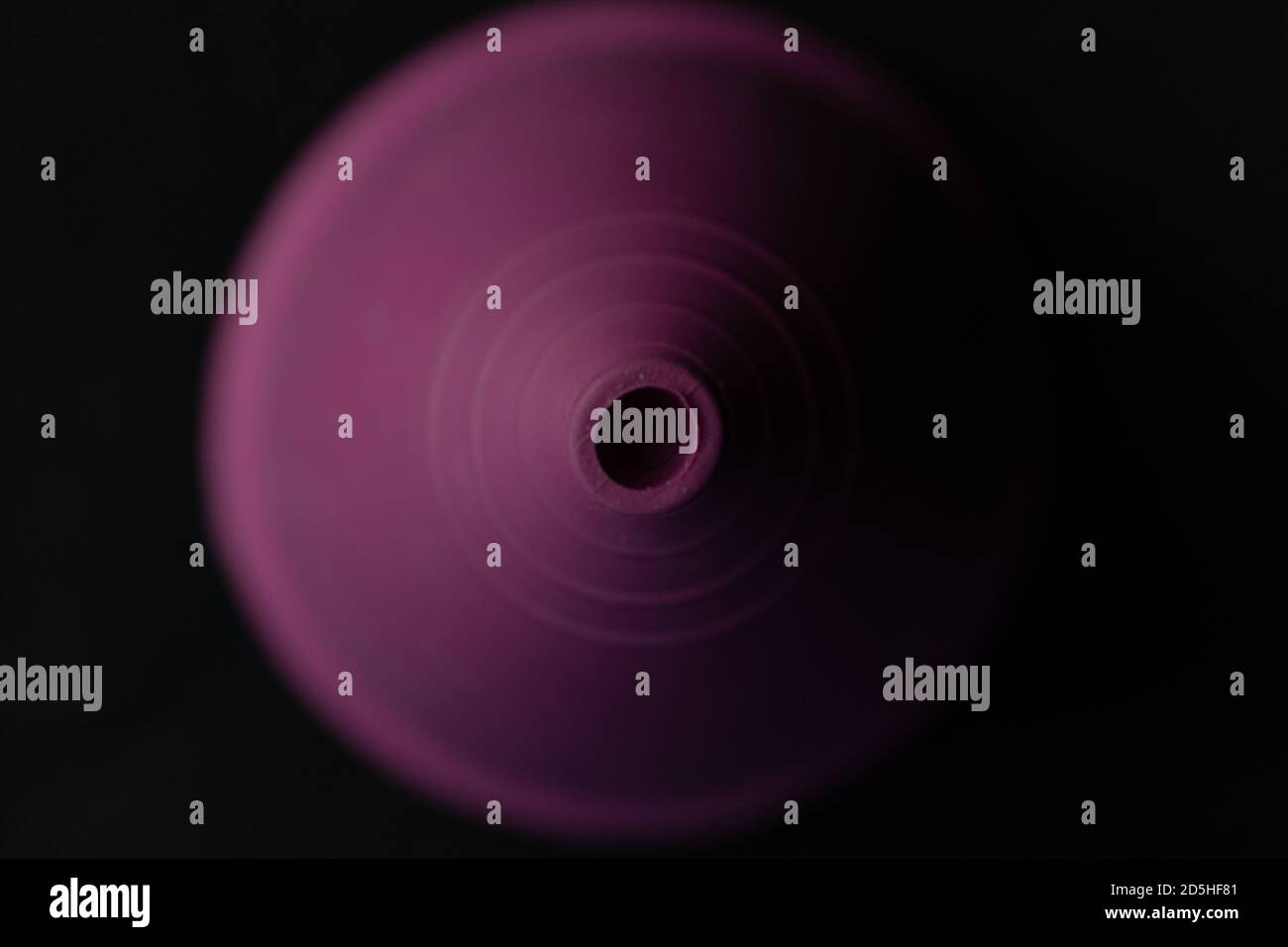 Overhead shot of the tube of a purple menstrual cup on black surface ...