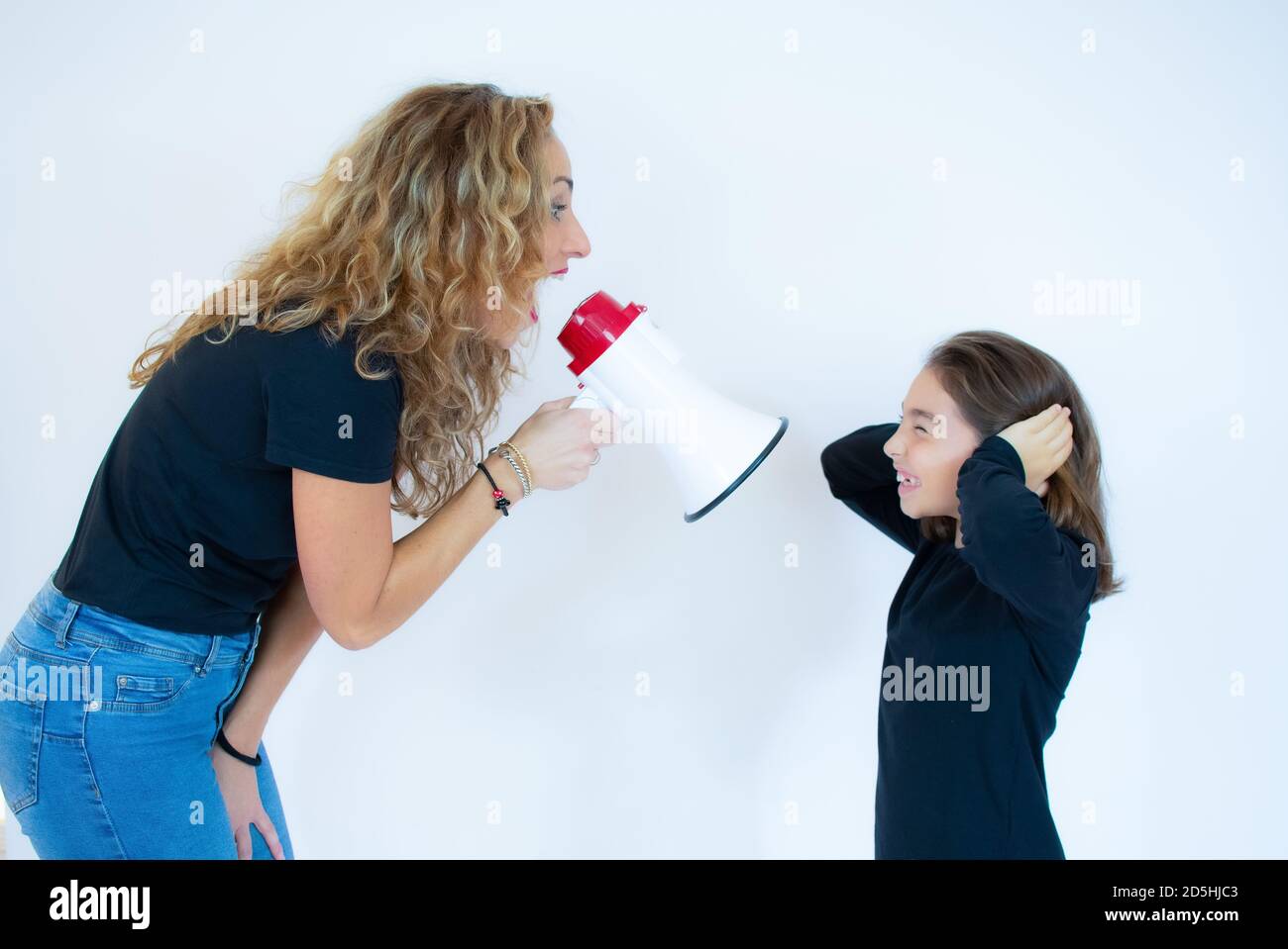 mother shouting at her daughter with a megaphone over white background ...