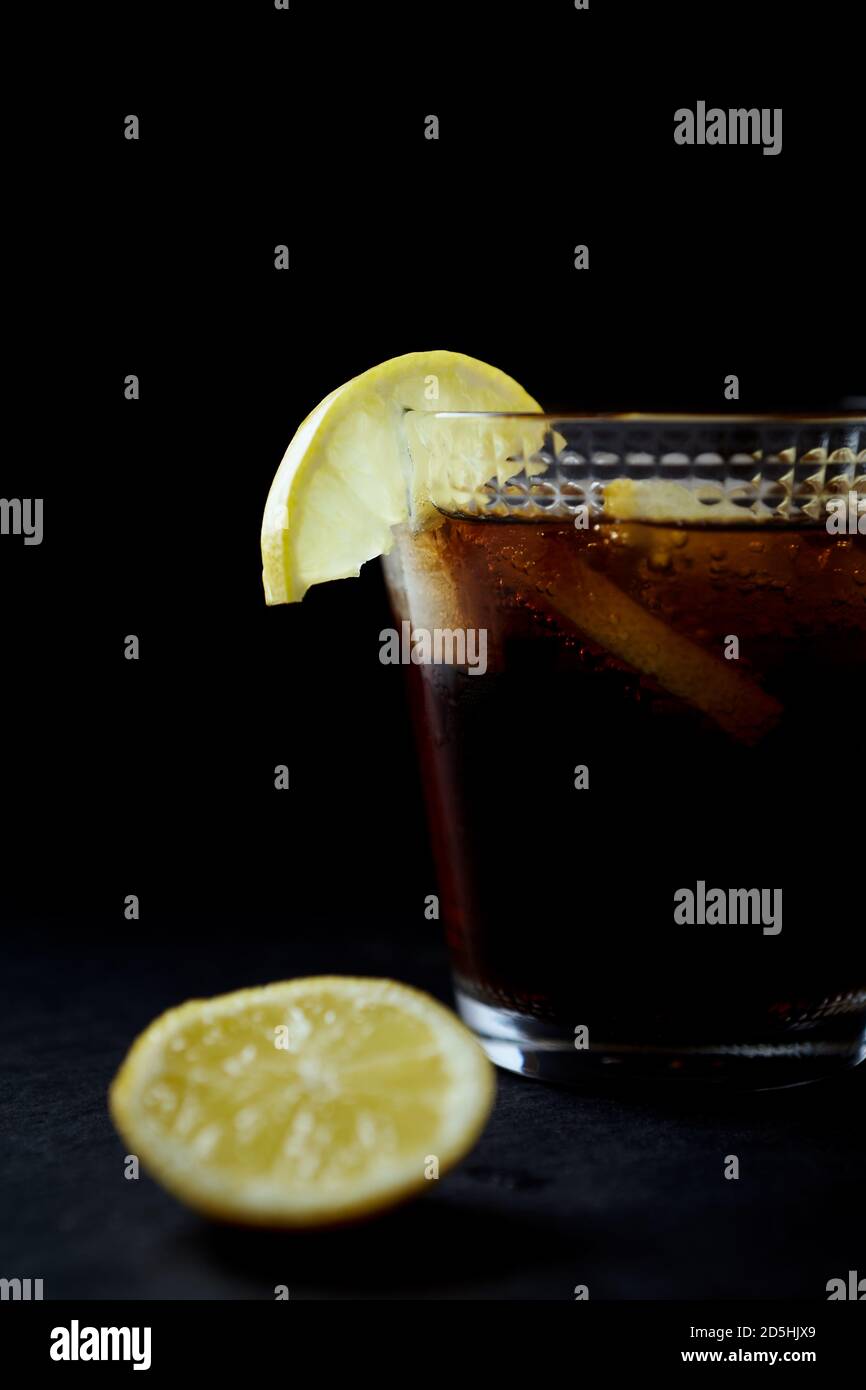 Glass of cola with lemon and ice cubes. Dark stone background. Close up ...