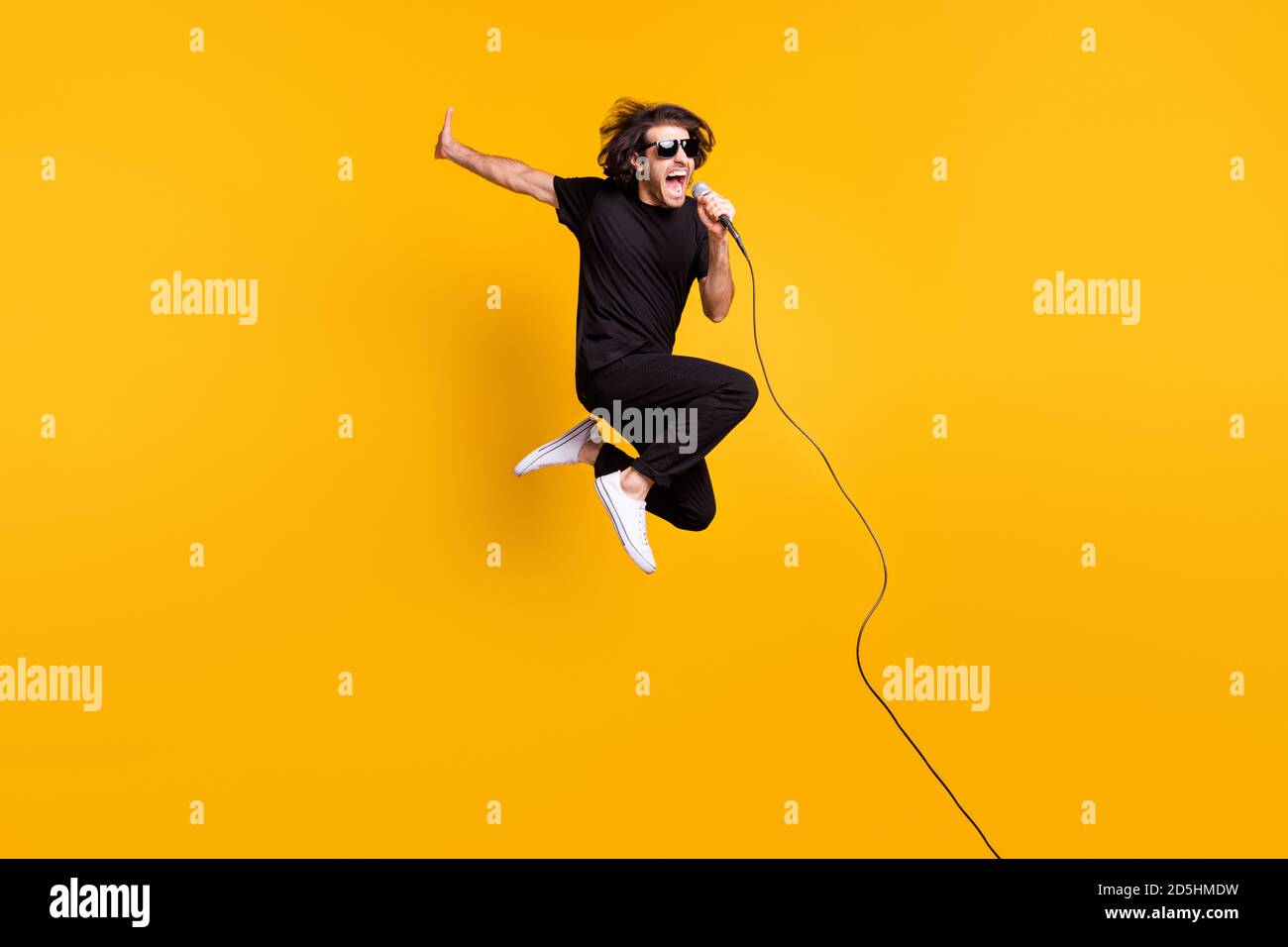 Full length photo of young man jump raise hand hold mic open mouth wear ...
