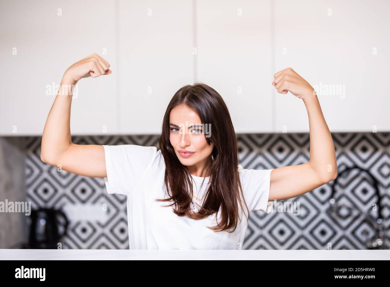 Young woman flexing muscles in the kitchen Stock Photo - Alamy