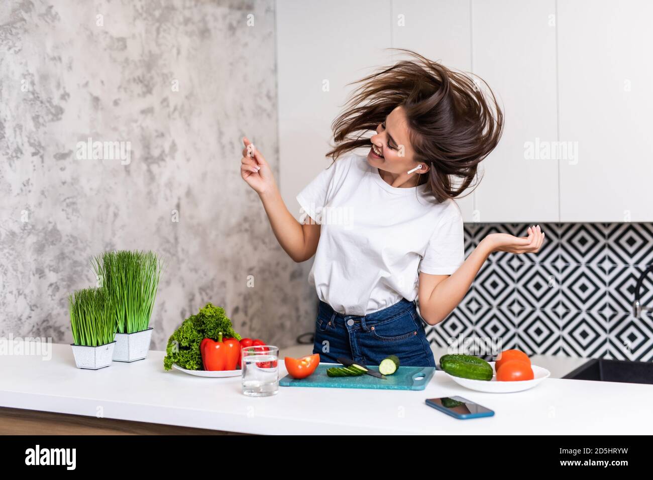 Beautiful woman listening to music and dancing while cooking in kitchen ...