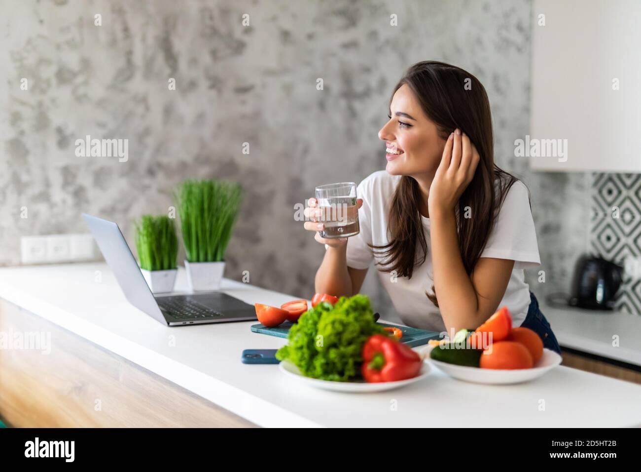 Beautiful woman in the white kitchen drinking water while cooking cozy ...