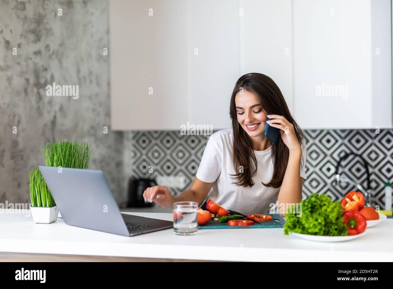 Happy excited woman talking on mobile phone while cooking in a kitchen ...