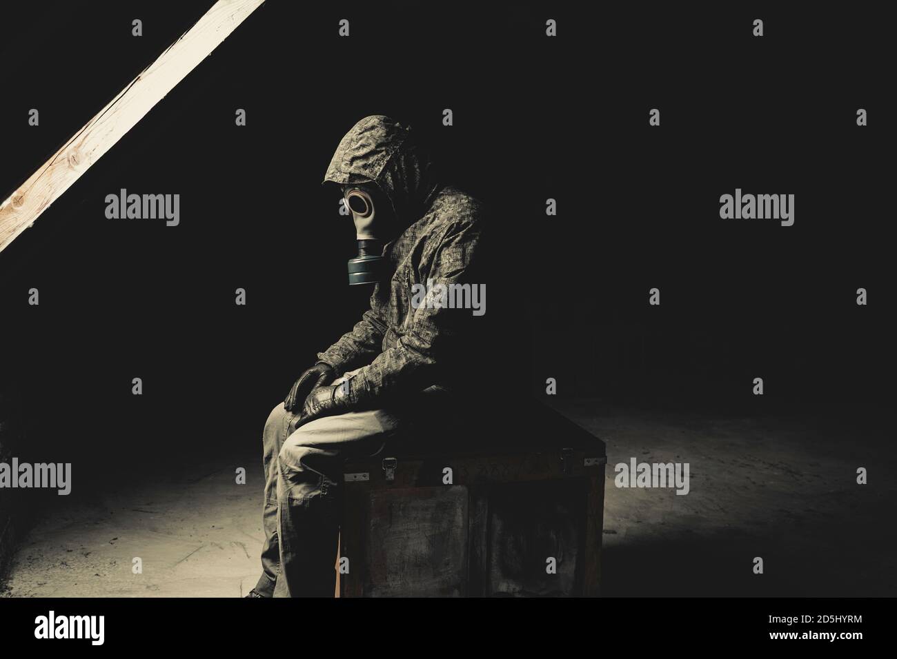 A sad man in gas mask and military-style clothes sitting on a wood box ...