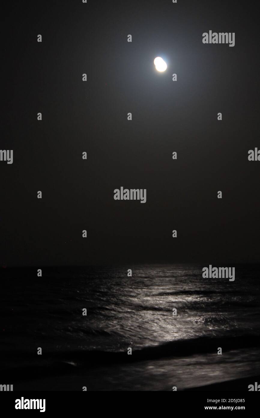 Moon rising over the ocean and causing a reflection back onto the water ...