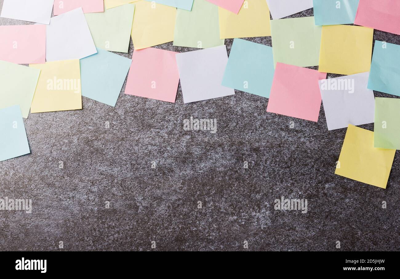 Many blank multicolored paper stick note list on concrete wall ...