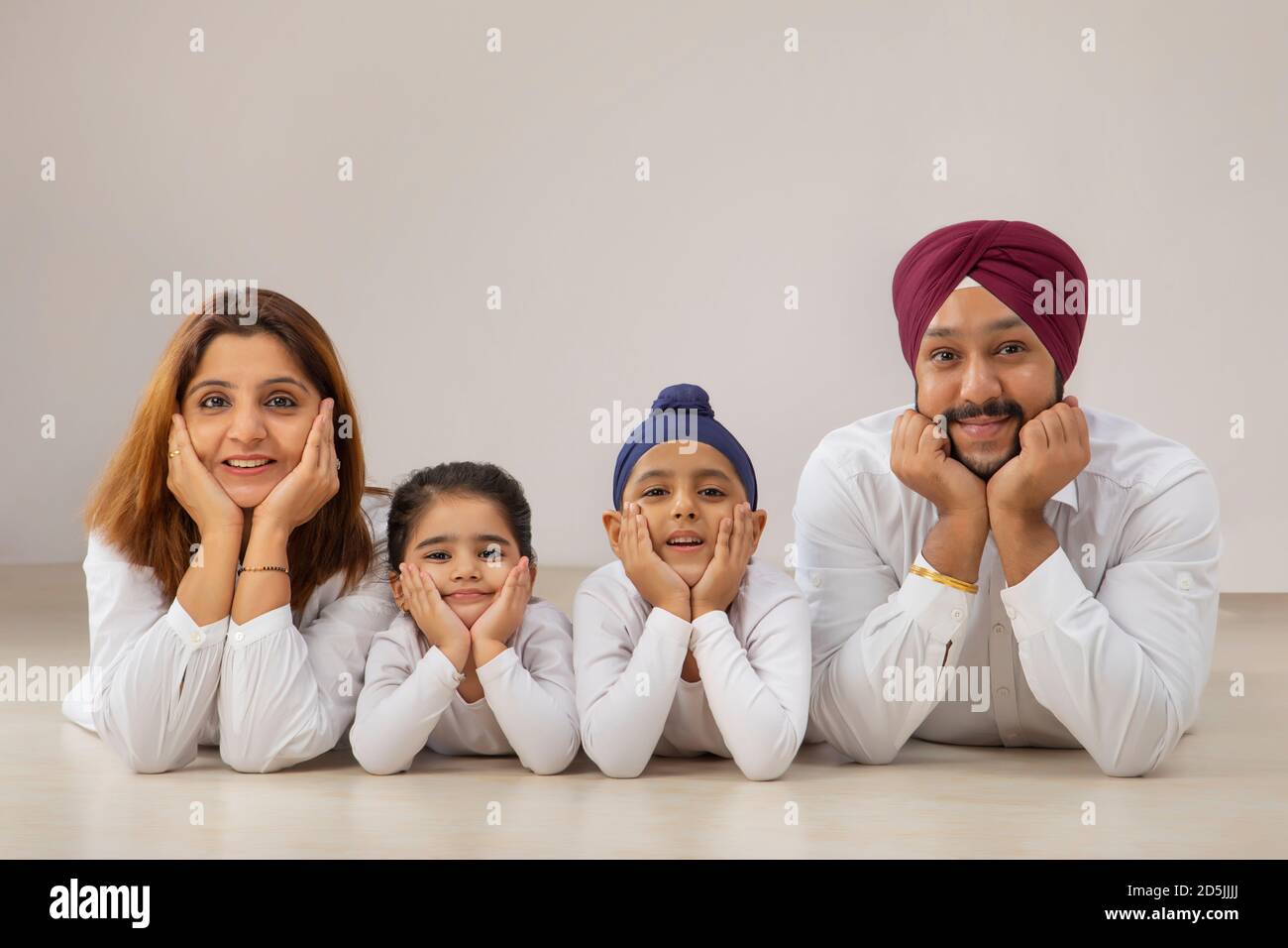 A HAPPY SIKH FAMILY SMILING AND POSING TOGETHER ON FLOOR WITH HANDS ON ...