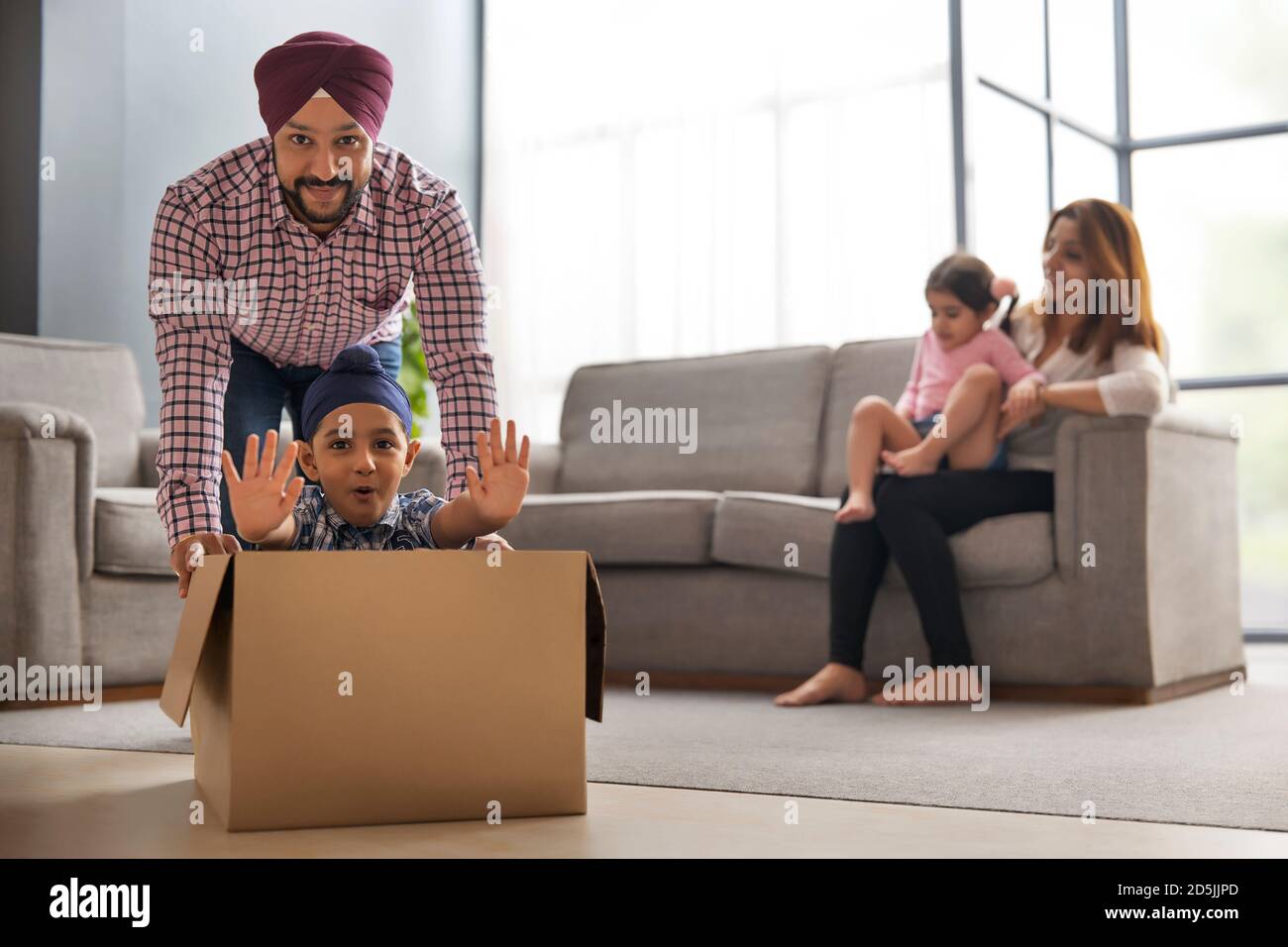 A SIKH FATHER AND SON PLAY WITH A CARDBOARD BOX WHILE MOTHER SITTING ON ...