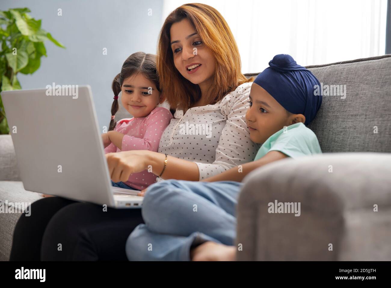 A SIKH MOTHER CHEERFULLY TEACHING HER SON AND DAUGHTER ON A LAPTOP AND ...