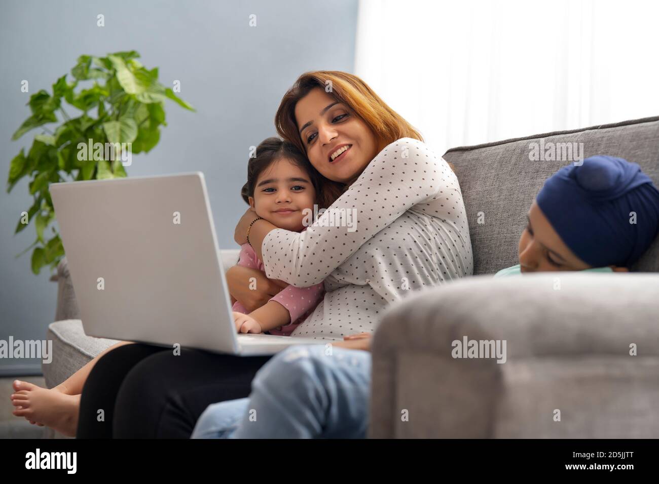 A SIKH MOTHER HUGGING HER DAUGHTER WITH BRIGHT SMILE WITH LAPTOP ON LAP ...