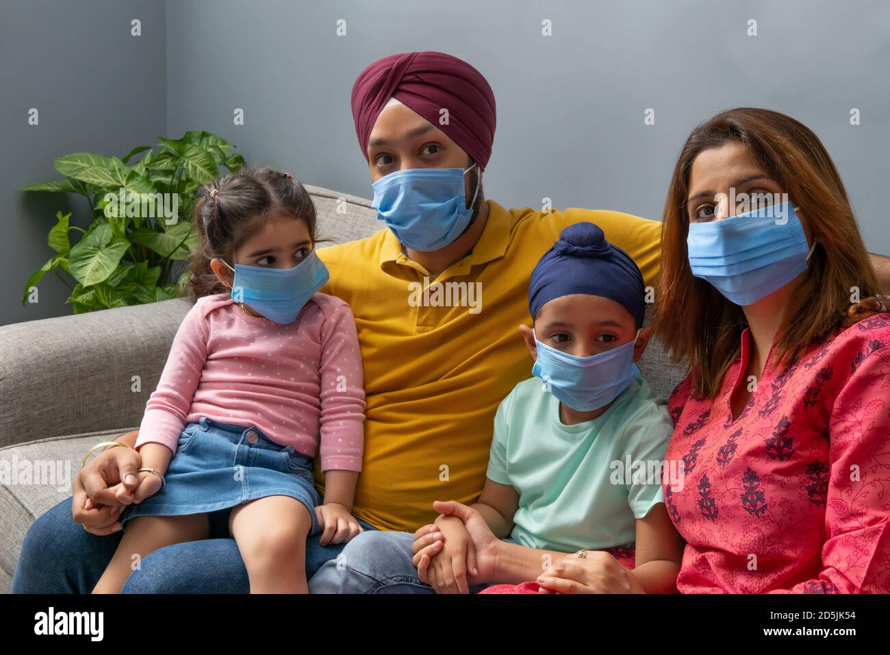 A SIKH FAMILY SITTING TOGETHER ON SOFA WITH MASKS AND LOOKING AT CAMERA ...